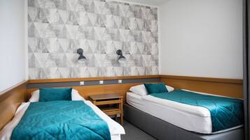 Quarto de hotel com duas camas, cabeceira de madeira, uma mesa pequena e parede com padrão geométrico.