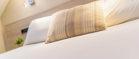 Cama bem arrumada com travesseiro listrado e luminária fixada na parede.