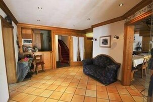 Ampla sala de estar com piso cerâmico, sofá, mesa de jantar e escada que dá acesso a outro cômodo.
