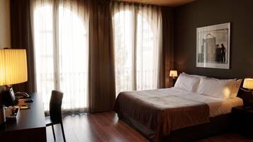 Quarto de hotel com cama, escrivaninha, cadeira e janela com cortinas.
