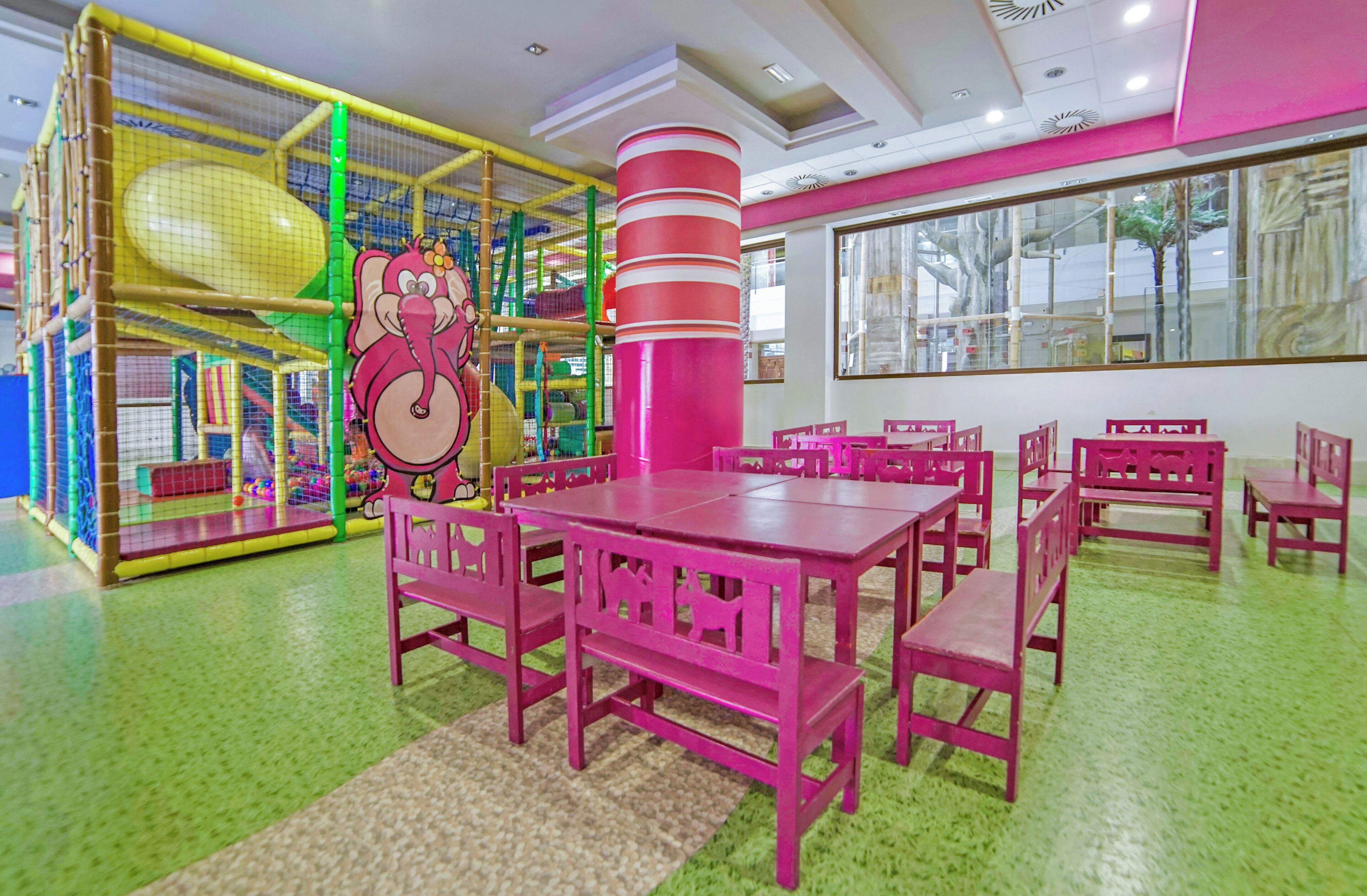 Uma área de recreação infantil com um escorregador inflável grande, uma estrutura de escalada e uma casinha cor-de-rosa.