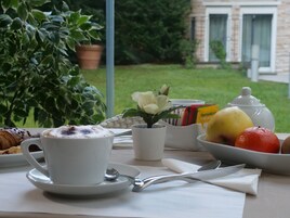 Uma mesa de café da manhã com uma xícara de café, um prato de croissants, uma tigela de frutas e um livro.