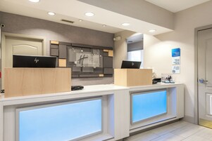 Balcão de recepção de hotel com dois laptops HP, um painel digital de entrada e saída e design de interiores moderno.