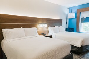 Quarto de hotel com duas camas, uma mesa de cabeceira, uma luminária e uma janela com vista.