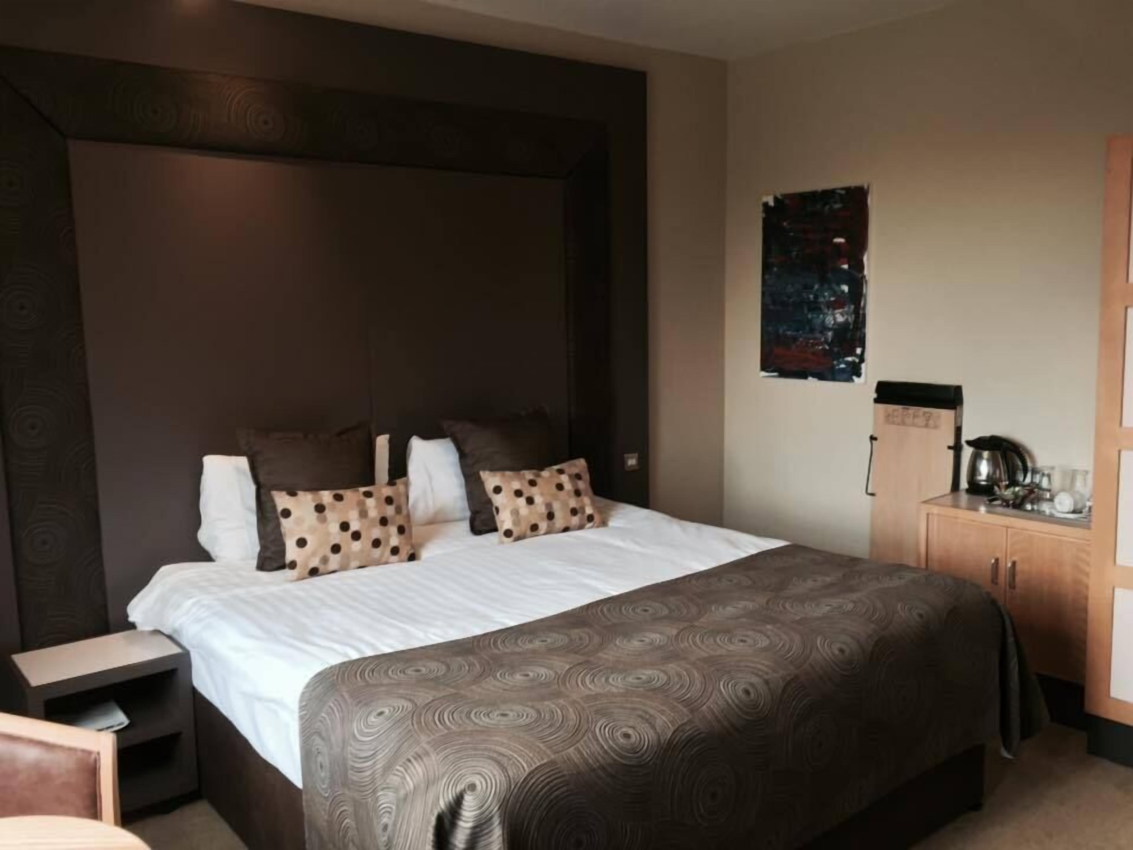 Quarto de hotel com uma cama grande, uma mesa de cabeceira, um guarda-roupa de madeira e um cartaz na parede.