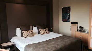 Quarto de hotel com uma cama grande, uma mesa de cabeceira, um guarda-roupa de madeira e um cartaz na parede.