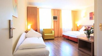 Quarto de hotel com duas camas, uma cadeira, uma televisão e uma mesa com um vaso de flores.