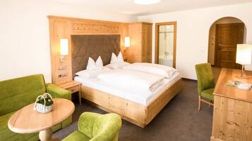 Quarto de hotel com cama de madeira, poltronas verdes, uma pequena mesa redonda e um armário de madeira.