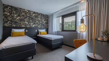 Quarto de hotel moderno com duas camas, uma escrivaninha, uma cadeira, uma janela grande e uma parede decorativa.