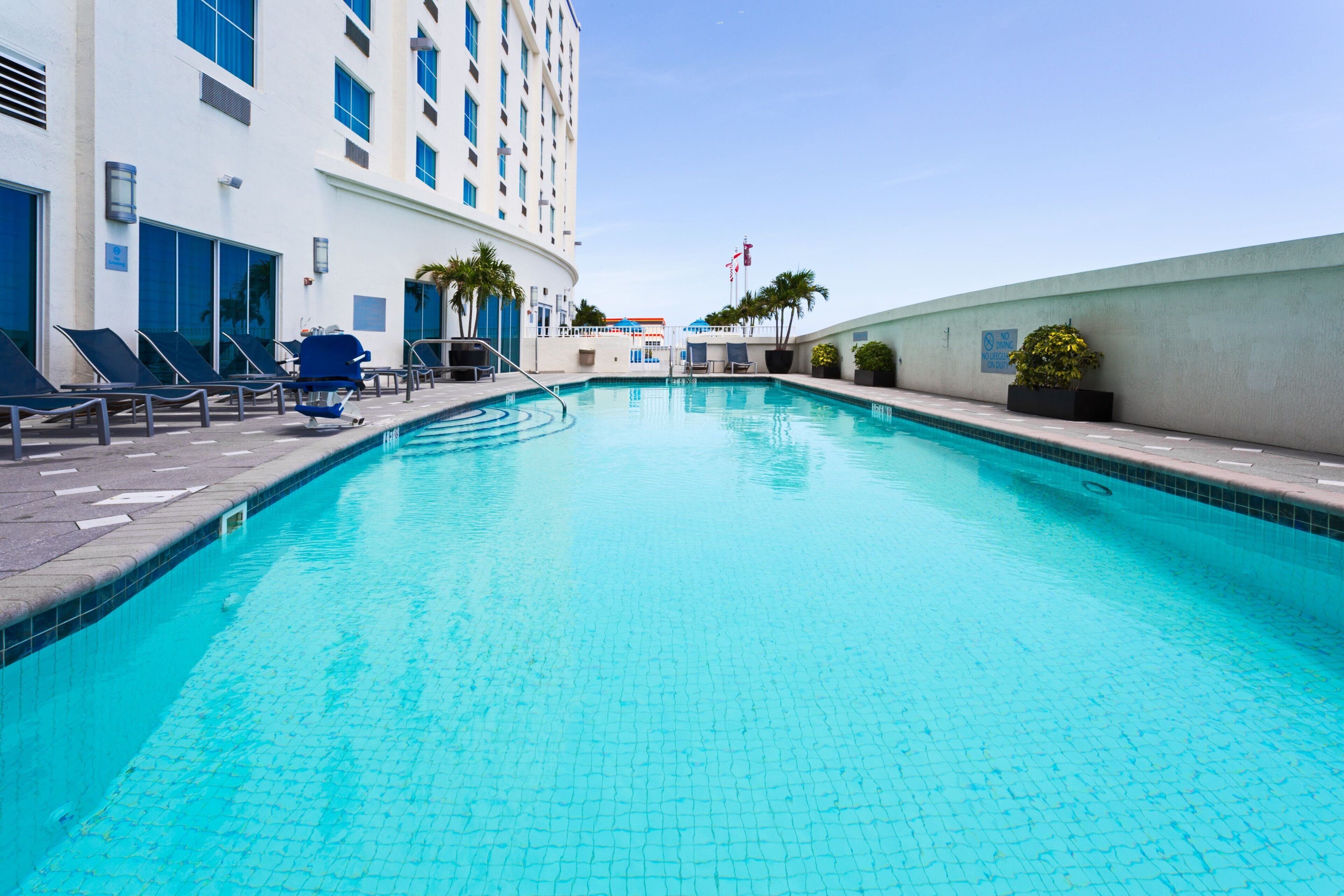 Piscina com espreguiçadeiras e um edifício ao fundo.
