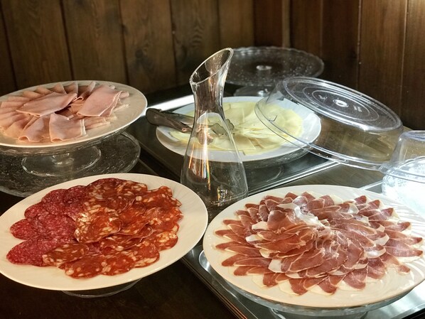 Uma mesa de buffet com diversos tipos de embutidos e queijos.