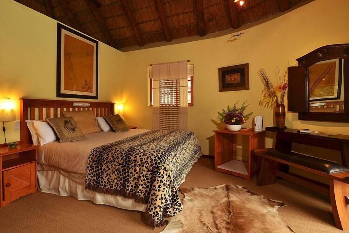 Quarto com cama, mesinhas de cabeceira de madeira, escrivaninha, espelho e uma grande pintura na parede.