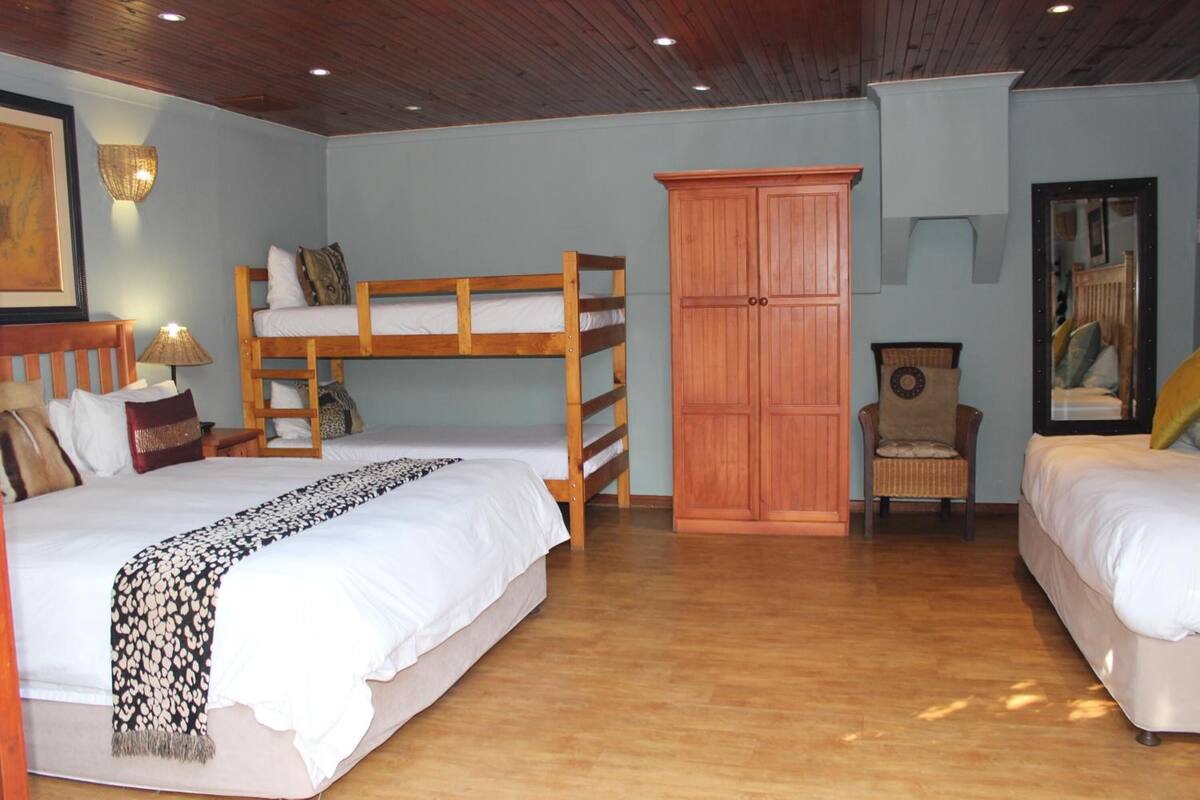 Quarto com duas camas, incluindo uma beliche de madeira, um guarda-roupa, uma cadeira e uma luminária fixada na parede.