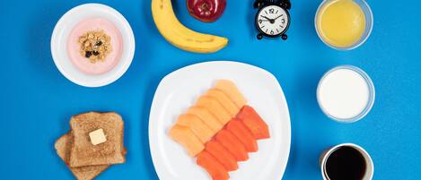 Café da manhã com torradas, frutas, iogurte e bebidas em fundo azul.