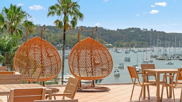Terraço com cadeiras e mesas de vime com vista para uma marina e barcos.