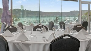 Espaço de refeições com mesas postas para uma refeição, grandes janelas com vista para a paisagem costeira.