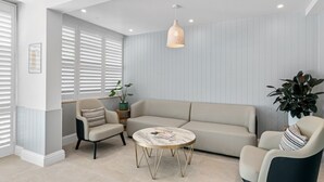 Uma sala de estar moderna com um sofá bege, duas poltronas, uma mesa de centro redonda e uma luminária pendente.
