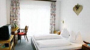 Quarto de hotel com cama, escrivaninha, cadeira e televisão.