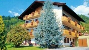 Edifício de vários andares com varandas, cercado por vegetação e um céu claro.