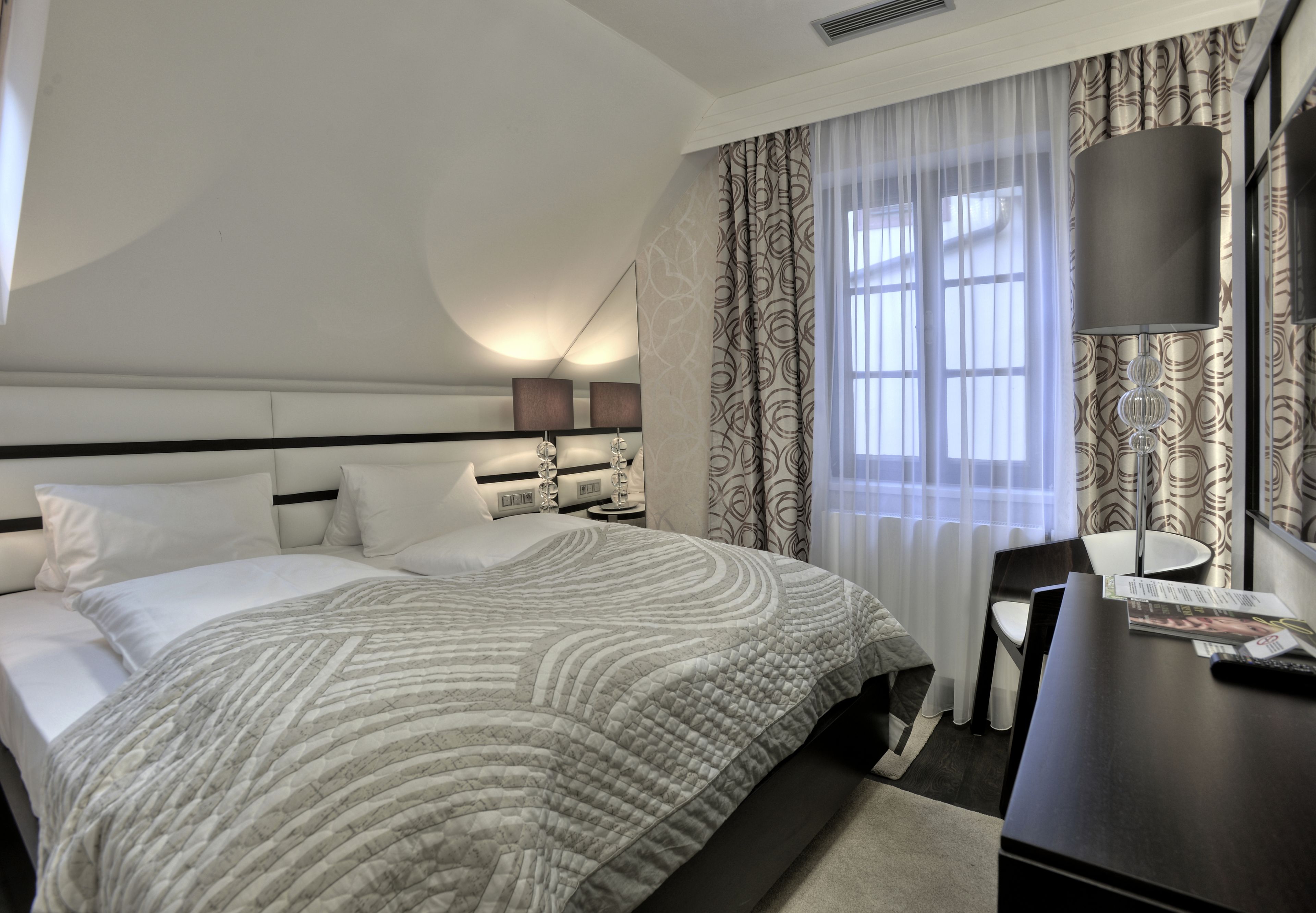 Quarto de hotel com uma cama grande, uma escrivaninha, uma cadeira e uma janela com cortinas.