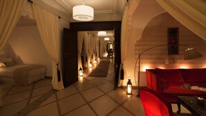 Corredor de hotel com um sofá vermelho, uma cama e um candelabro.