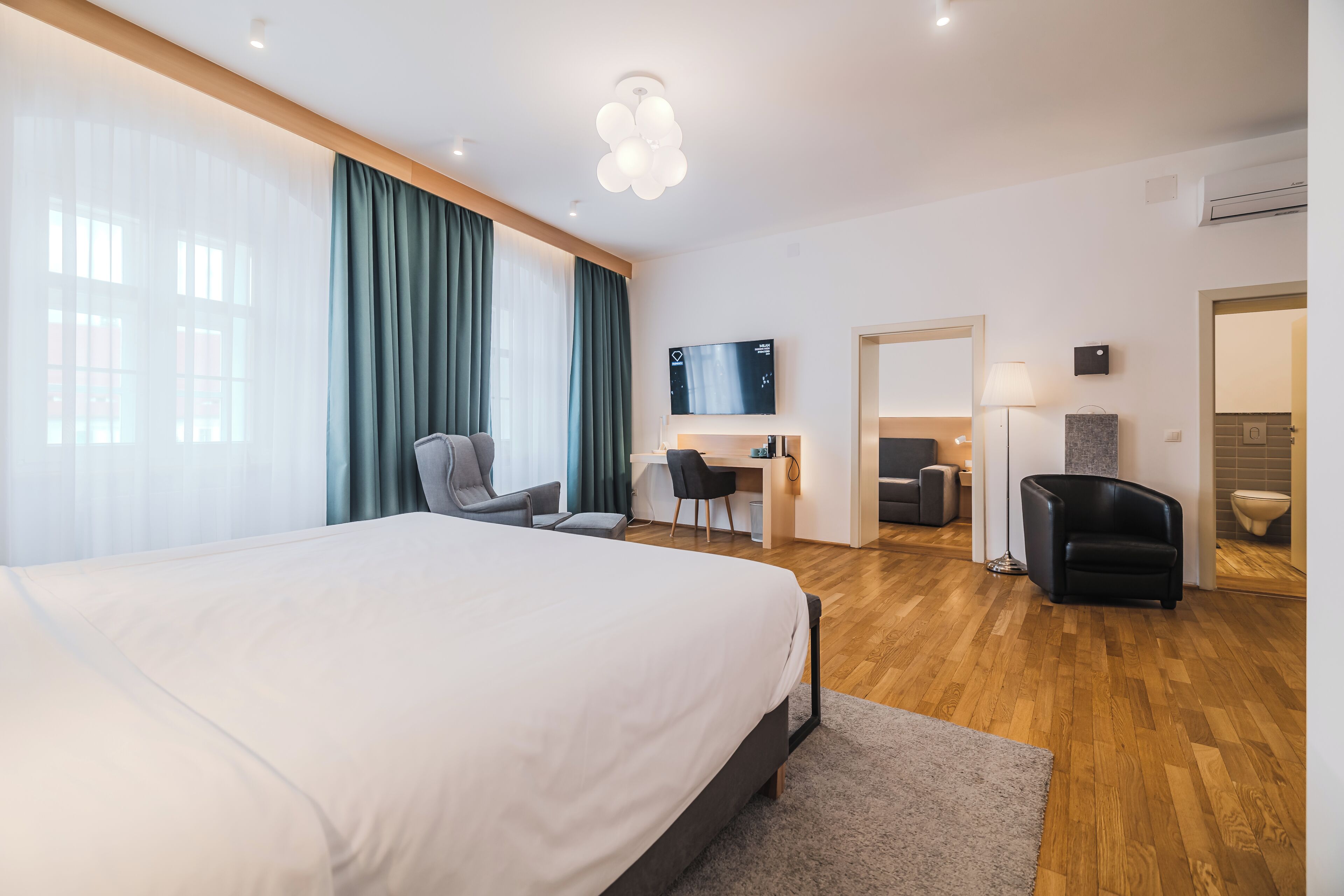 Quarto de hotel com uma cama grande, uma escrivaninha, uma cadeira, televisão e banheiro.
