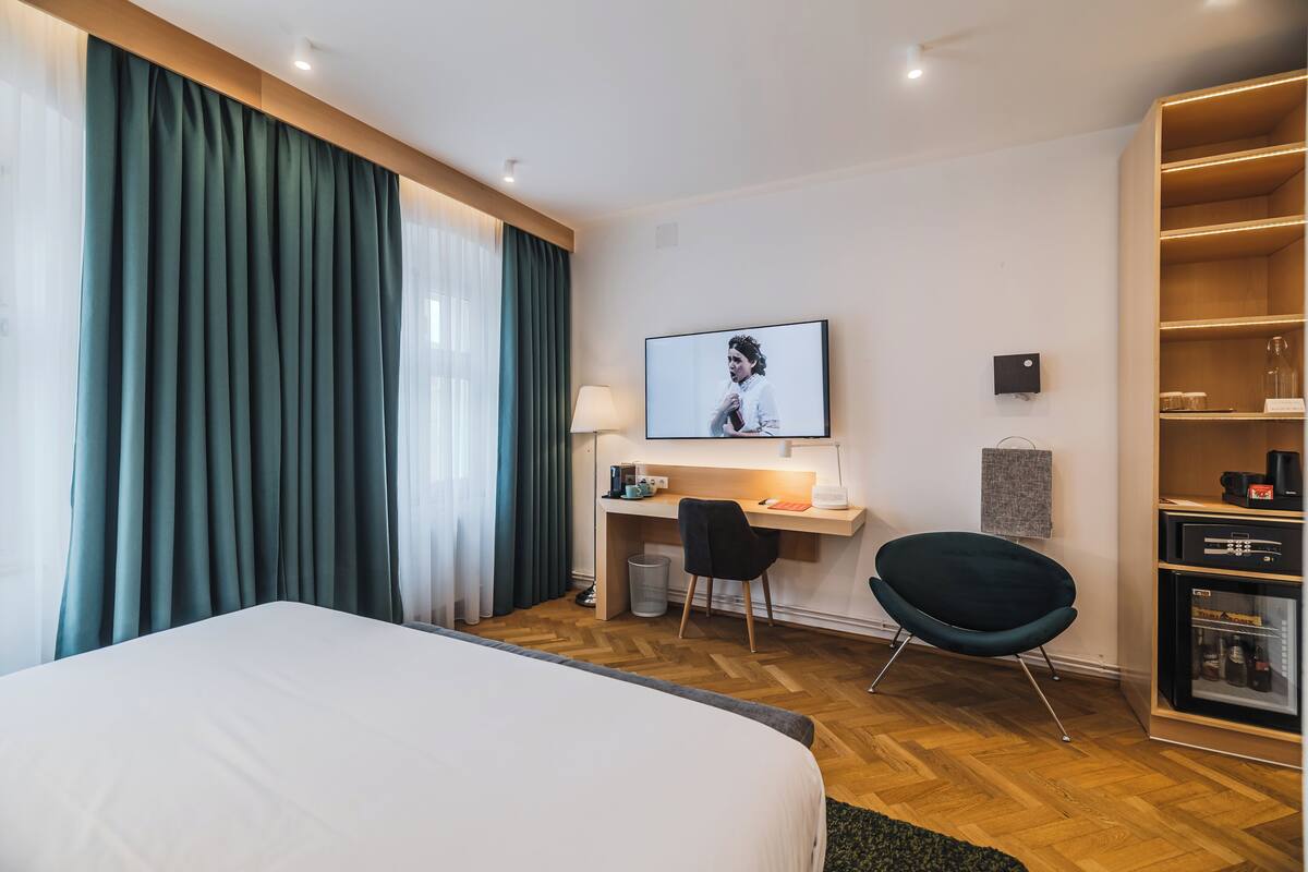 Quarto de hotel com cama, escrivaninha, cadeira, televisão e minibar.