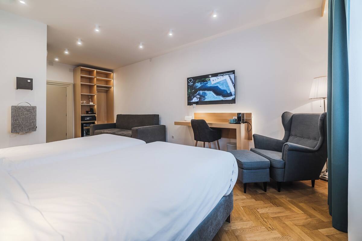 Quarto de hotel moderno com uma cama grande, uma escrivaninha, duas cadeiras, uma televisão e um guarda-roupa.