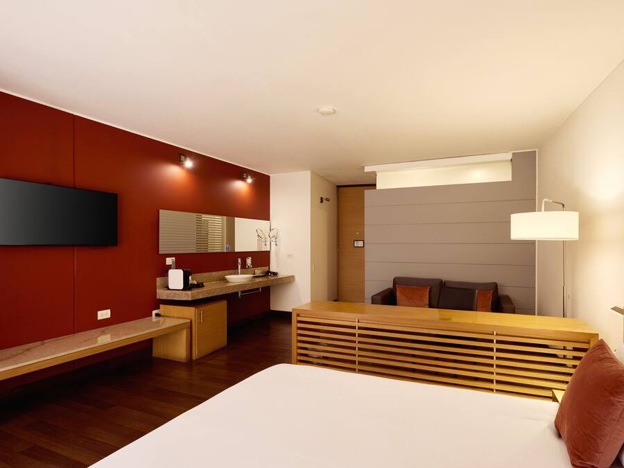 Quarto de hotel moderno com cama, escrivaninha, televisão, banheiro e área de estar.