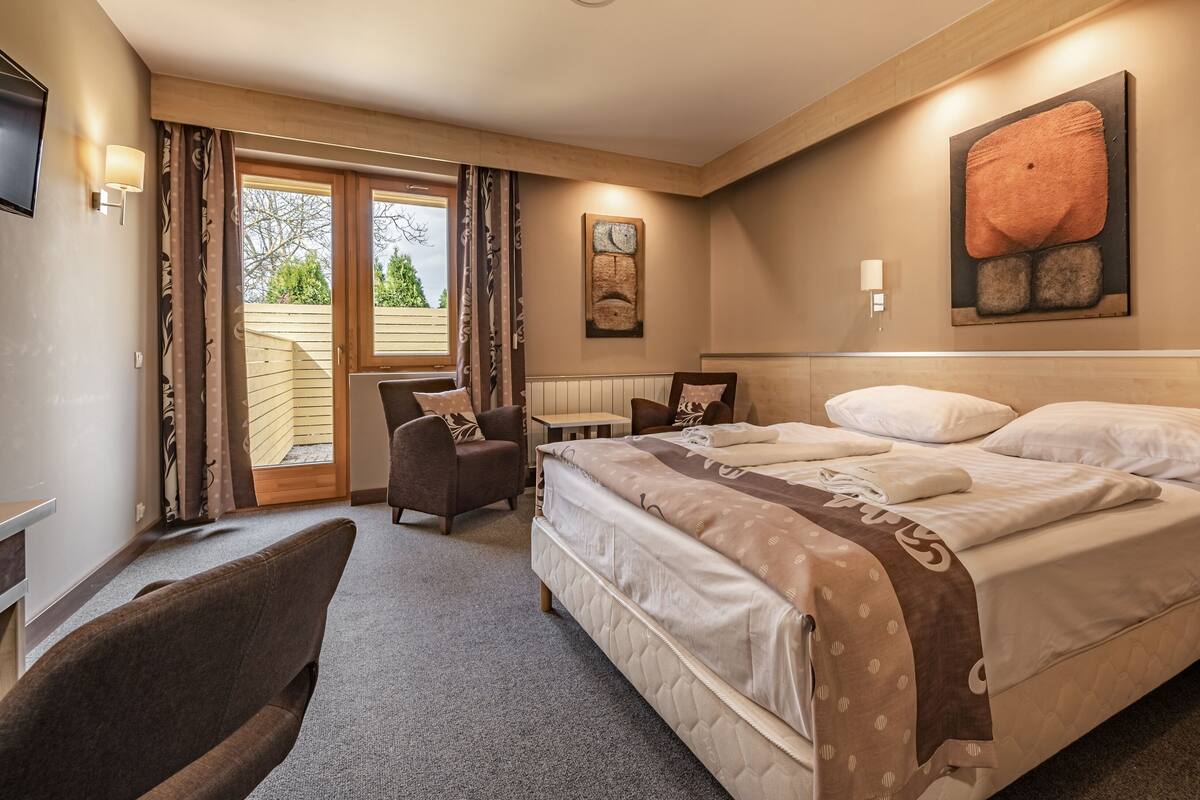 Quarto de hotel com cama, cadeira, mesa e janela com cortinas.