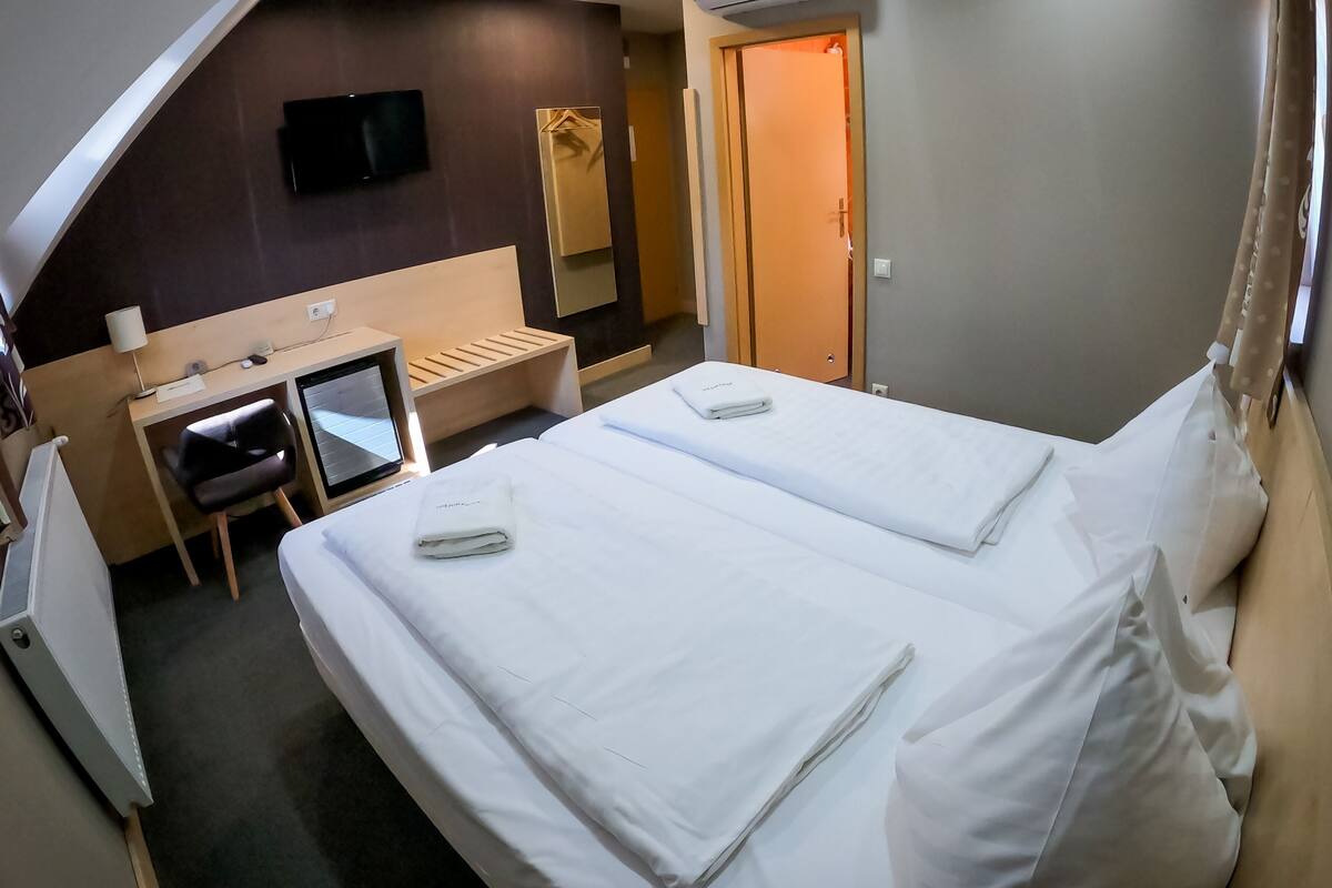 Quarto de hotel com duas camas, uma escrivaninha, uma cadeira, uma televisão e um espelho.