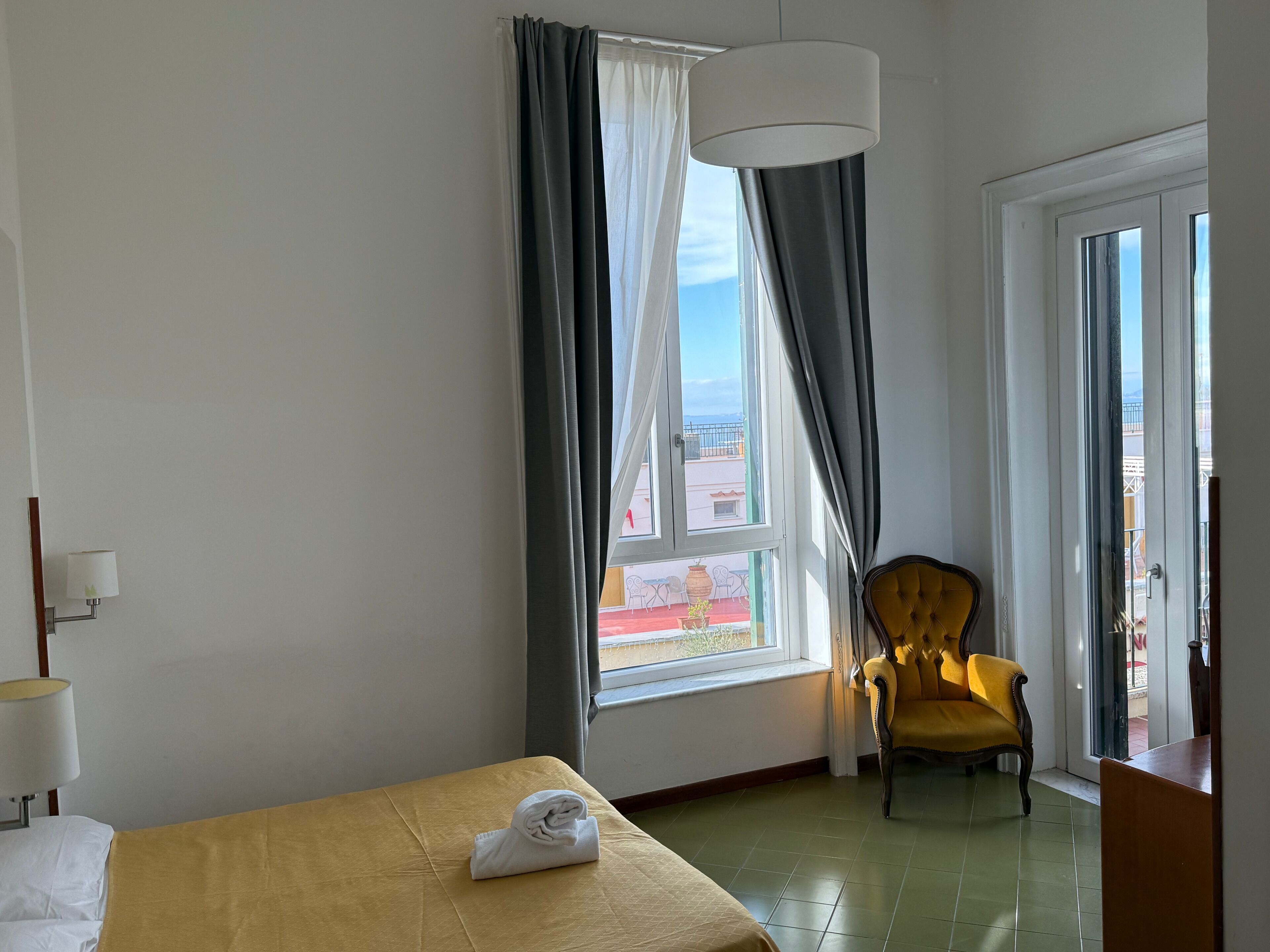 Quarto de hotel com uma cama, uma cadeira, uma janela com cortinas e vista para o exterior.