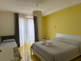 Quarto de hotel com duas camas de solteiro, uma mesinha branca, uma cadeira, um abajur e uma janela com cortinas.