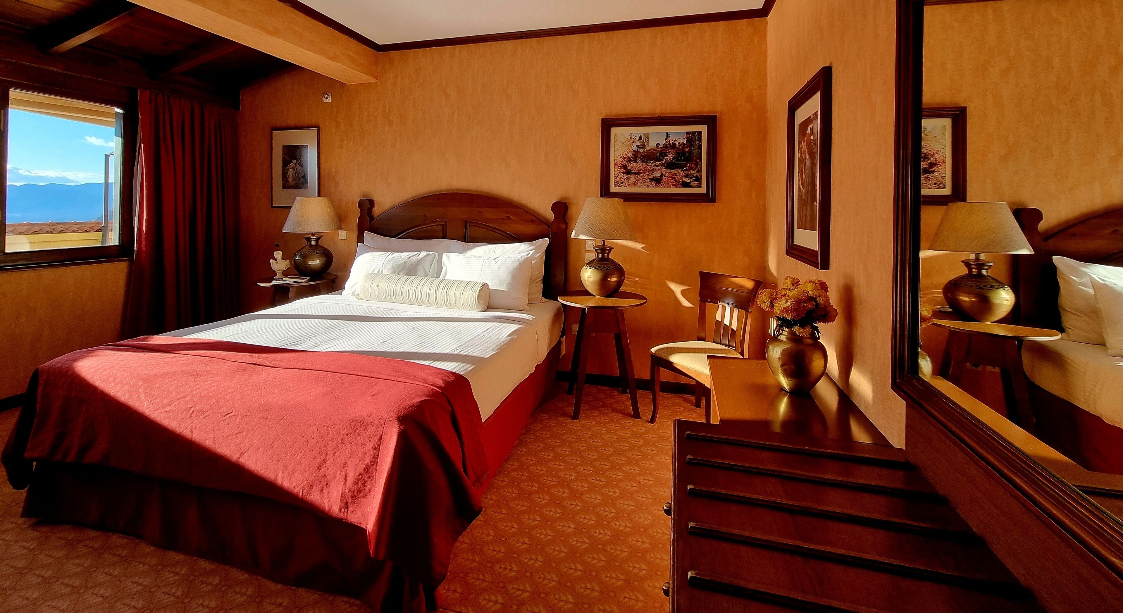 Quarto de hotel com uma cama grande, duas mesas de cabeceira com abajures, uma cadeira, uma escrivaninha e um espelho.