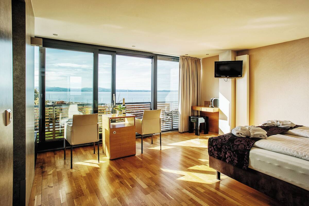 Quarto de hotel com uma janela grande, uma cama, uma mesa e uma televisão.