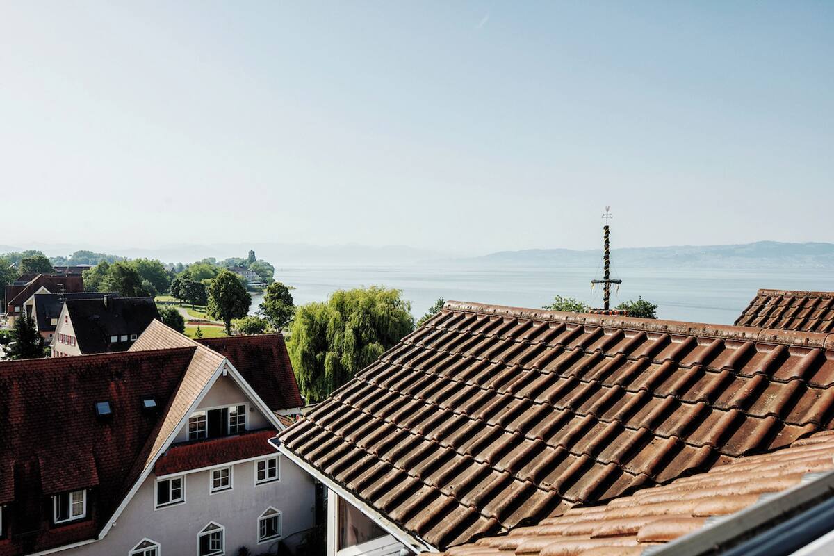 Vista de uma área residencial com telhados de telha de barro, um campanário de igreja e um corpo d'água ao longe.