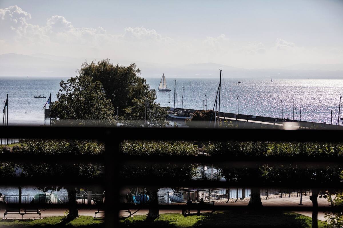 Um parque à beira-mar com um caminho para pedestres, bancos e vista para o mar com barcos.