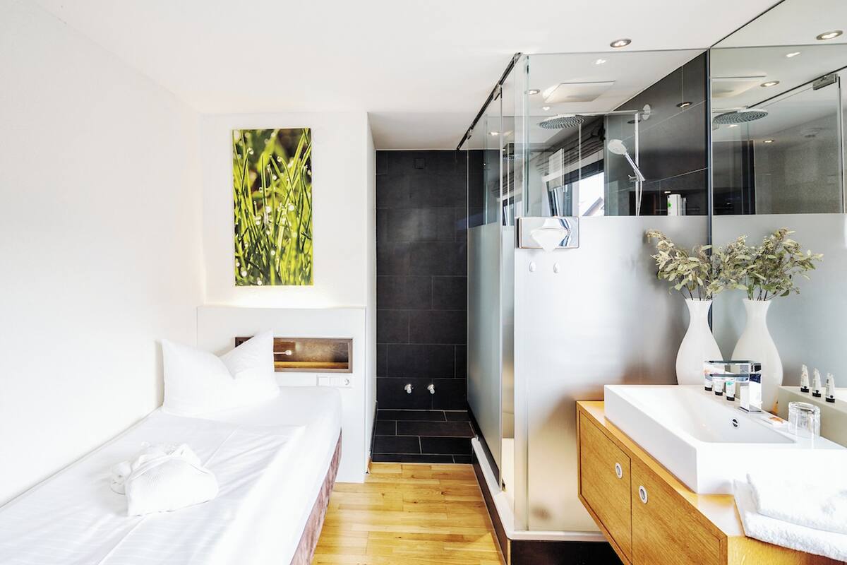 Quarto de hotel moderno com uma cama, um espelho grande, uma toucador com pia e zona de chuveiro.