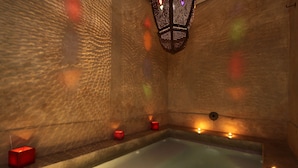Um quarto de spa com banheira, paredes texturizadas e velas vermelhas.