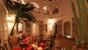 Uma sala de jantar com uma mesa posta para quatro pessoas, rodeada por cadeiras, uma planta grande e um cacto.