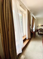 Quarto de hotel com uma janela grande, um banco de madeira, uma mesa de jantar e uma cadeira.
