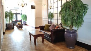 Um hall com piso de parquet de madeira, sofás de couro, uma mesa de centro, plantas em vasos e um candelabro.