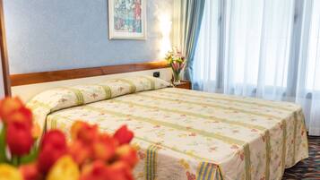 Quarto de hotel com uma cama, uma mesinha de cabeceira, um vaso com flores e um quadro na parede.