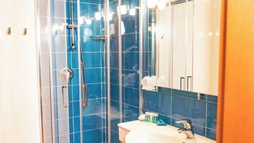 Uma casa de banho com chuveiro envidraçado, lavatório com espelho e paredes azulejadas em tons de azul.