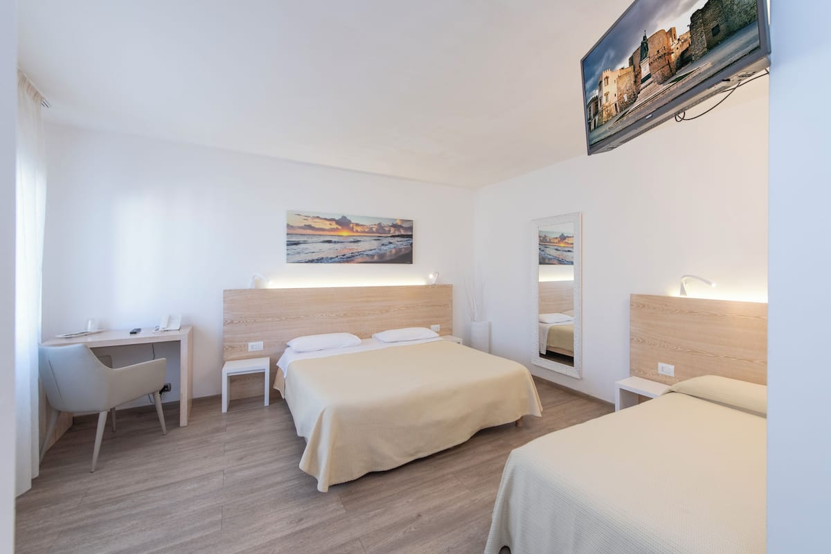 Quarto de hotel com cama, escrivaninha, cadeira e um quadro na parede.