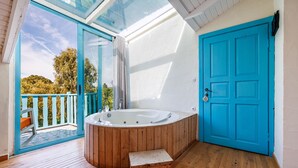 Um deck de madeira com uma banheira de hidromassagem, uma porta azul e vista para árvores.