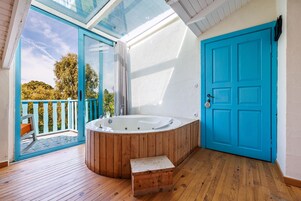 Um deck de madeira com uma banheira de hidromassagem, uma porta azul e vista para árvores.
