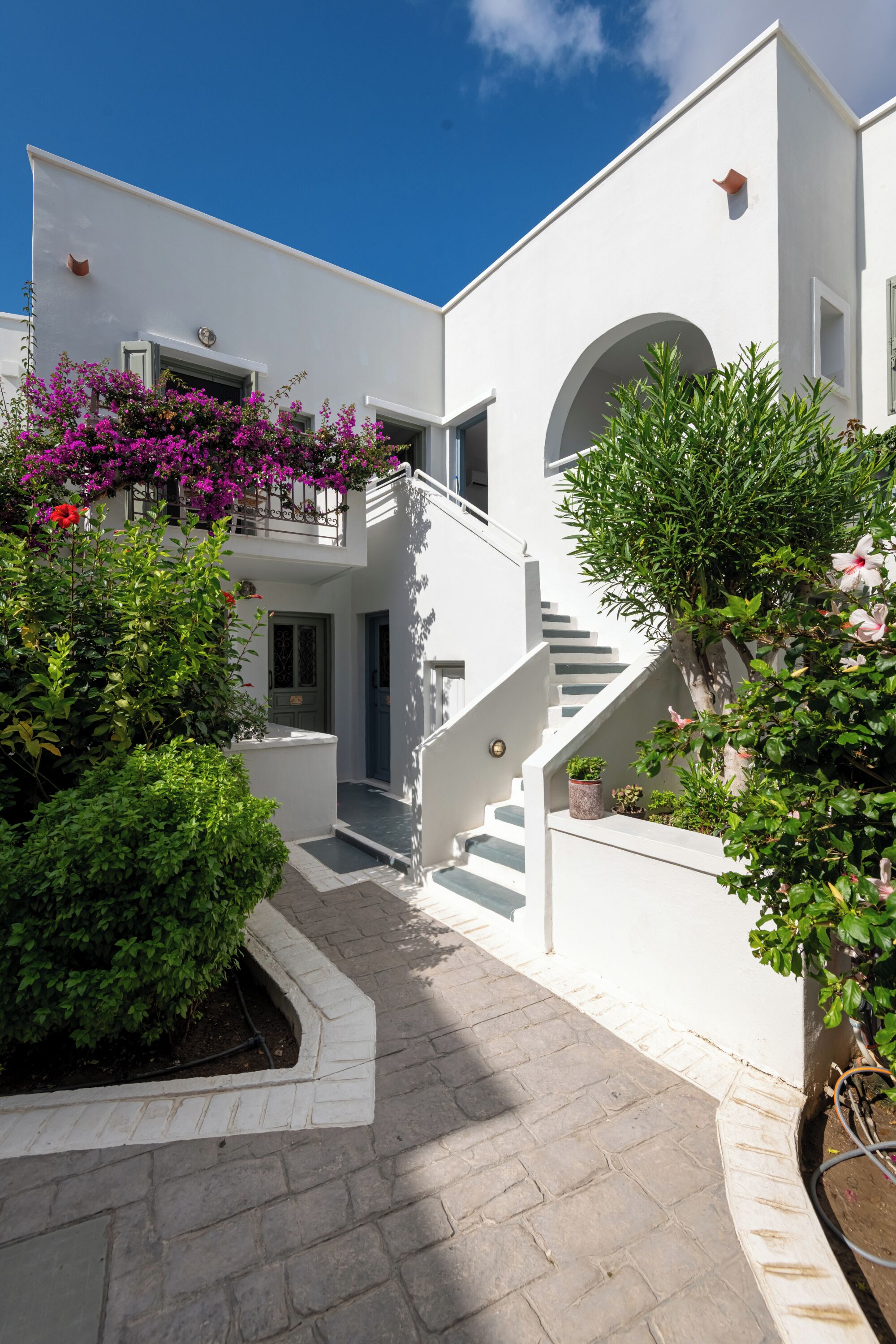 Um edifício moderno e branco com uma escadaria, uma pequena área de jardim e um céu azul claro.