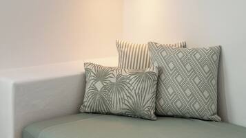 Canto de um quarto com um sofá verde, duas almofadas estampadas e duas luminárias pendentes.