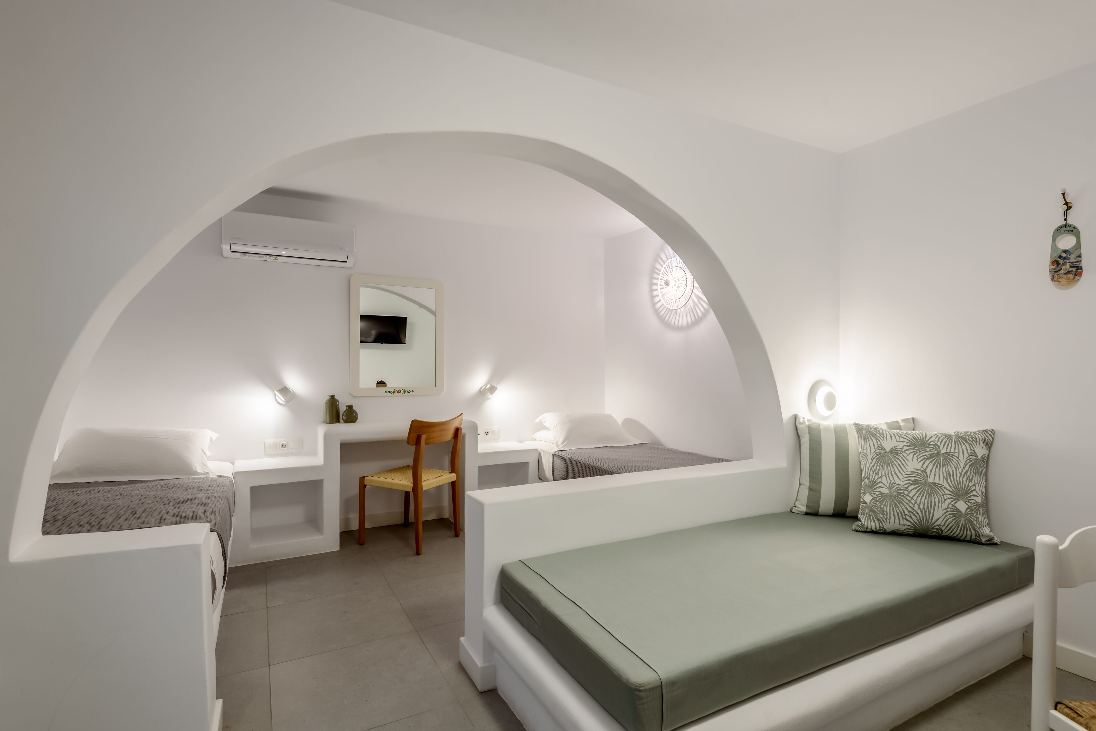 Quarto compacto com cama, escrivaninha, cadeira e uma pequena mesa.